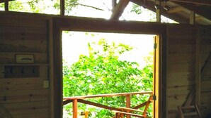 Uma cabana de madeira com varanda, soalho de madeira e uma cama com colcha estampada.