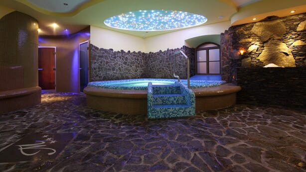Uma área de spa com piso de pedra, uma banheira de hidromassagem central e parede de pedra.