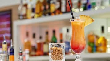 Ambiente de bar com um cocktail num copo alto e um copo pequeno com guarnição de fruta.