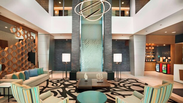 Um lobby moderno com área de estar central, painel decorativo e uma kitchenette visível.