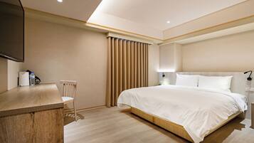 Quarto de hotel moderno com escrivaninha de madeira, uma cama de solteiro e televisão fixada na parede.