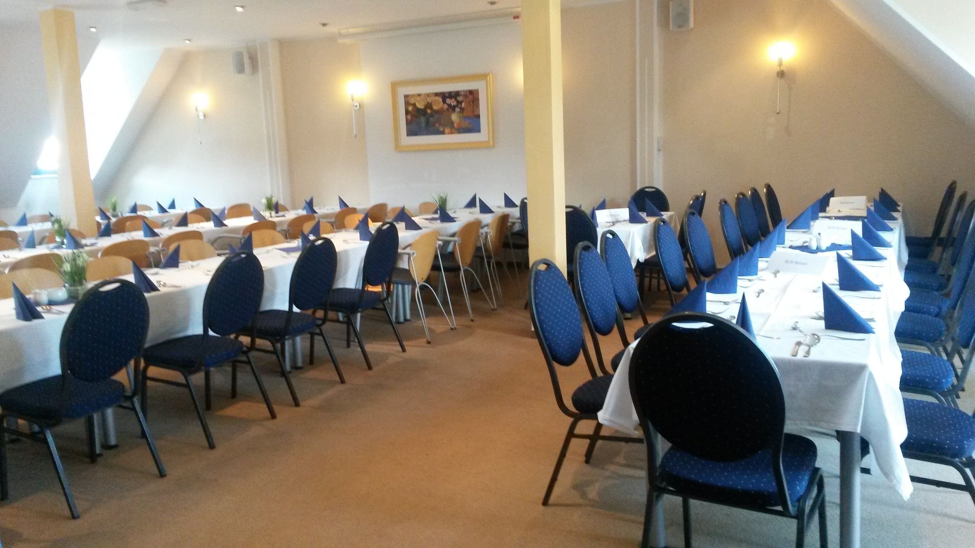 Uma sala de conferências com mesas e cadeiras dispostas em fileiras, preparada para uma reunião ou evento.