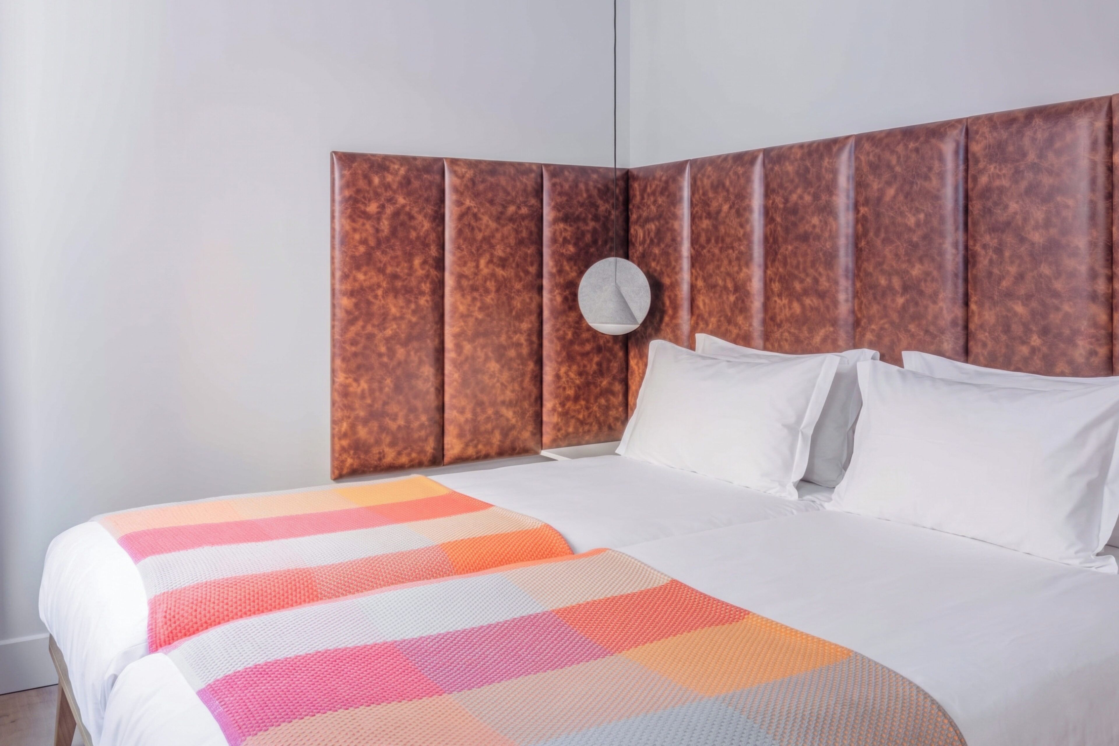 Quarto de hotel com uma cama, cabeceira e espelho redondo fixado na parede.