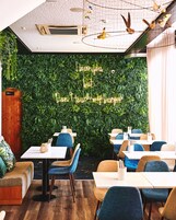 Interior de restaurante com parede verde, mobiliário de madeira e um letreiro de neon.