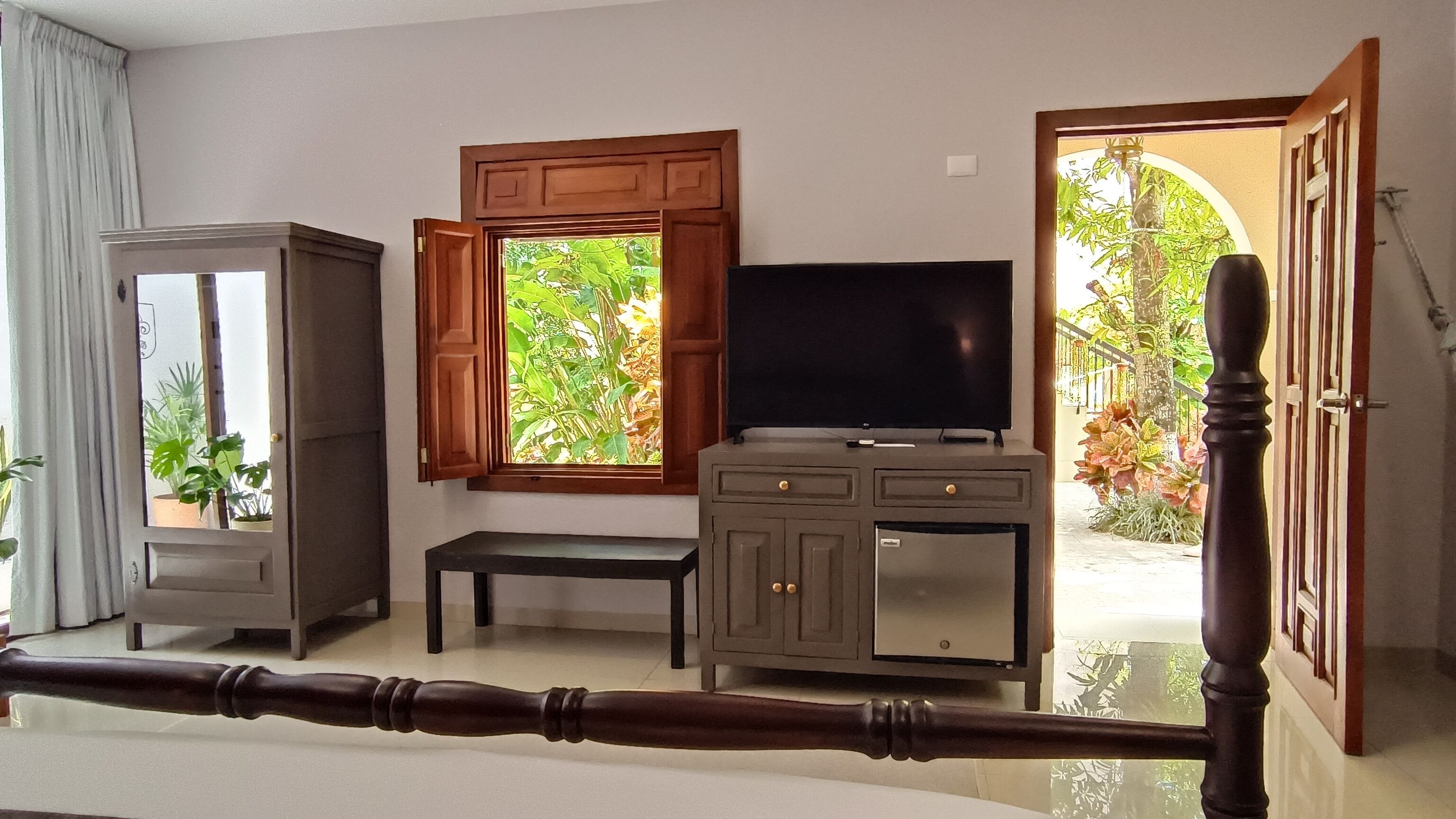 Um quarto com televisão sobre um armário, um banco e um guarda-roupa.