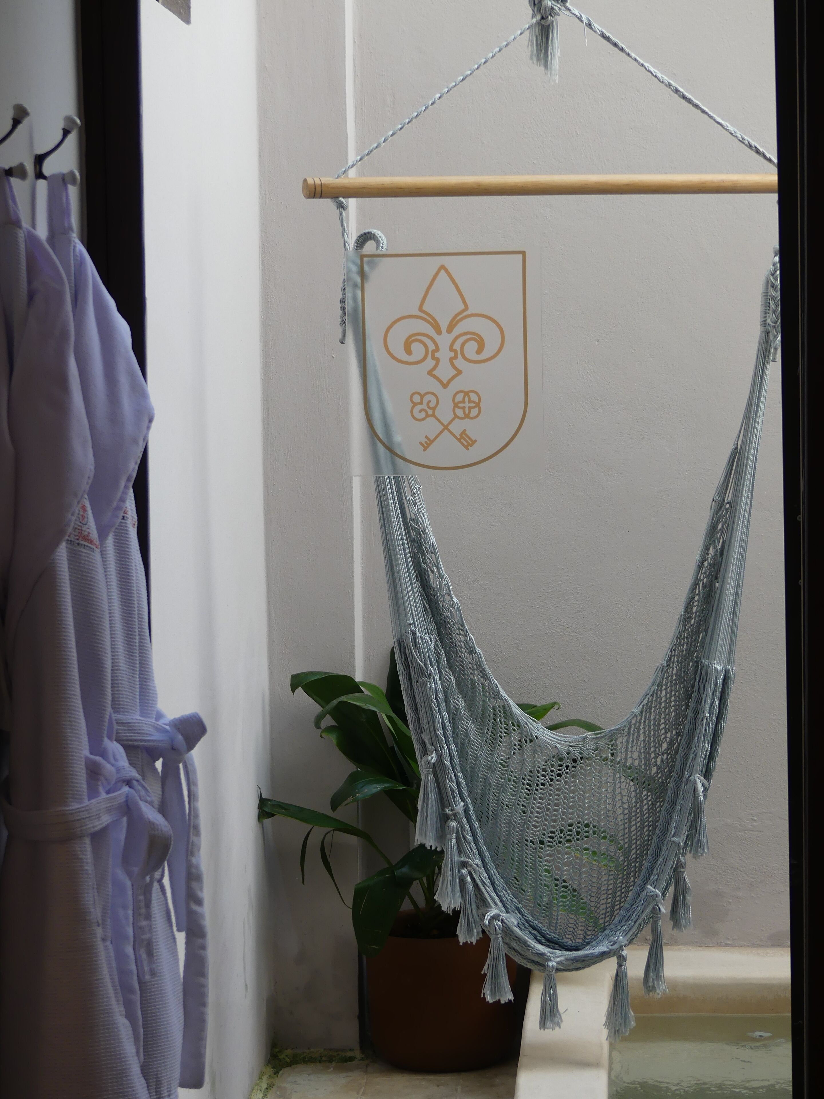 Uma rede pendurada em uma viga de madeira, um vaso com planta e um suporte com toalhas.