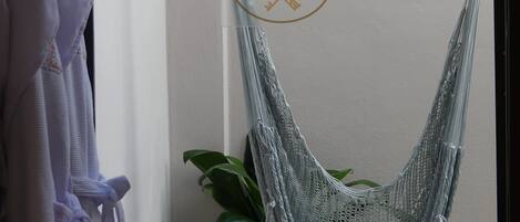 Uma rede pendurada em uma viga de madeira, um vaso com planta e um suporte com toalhas.