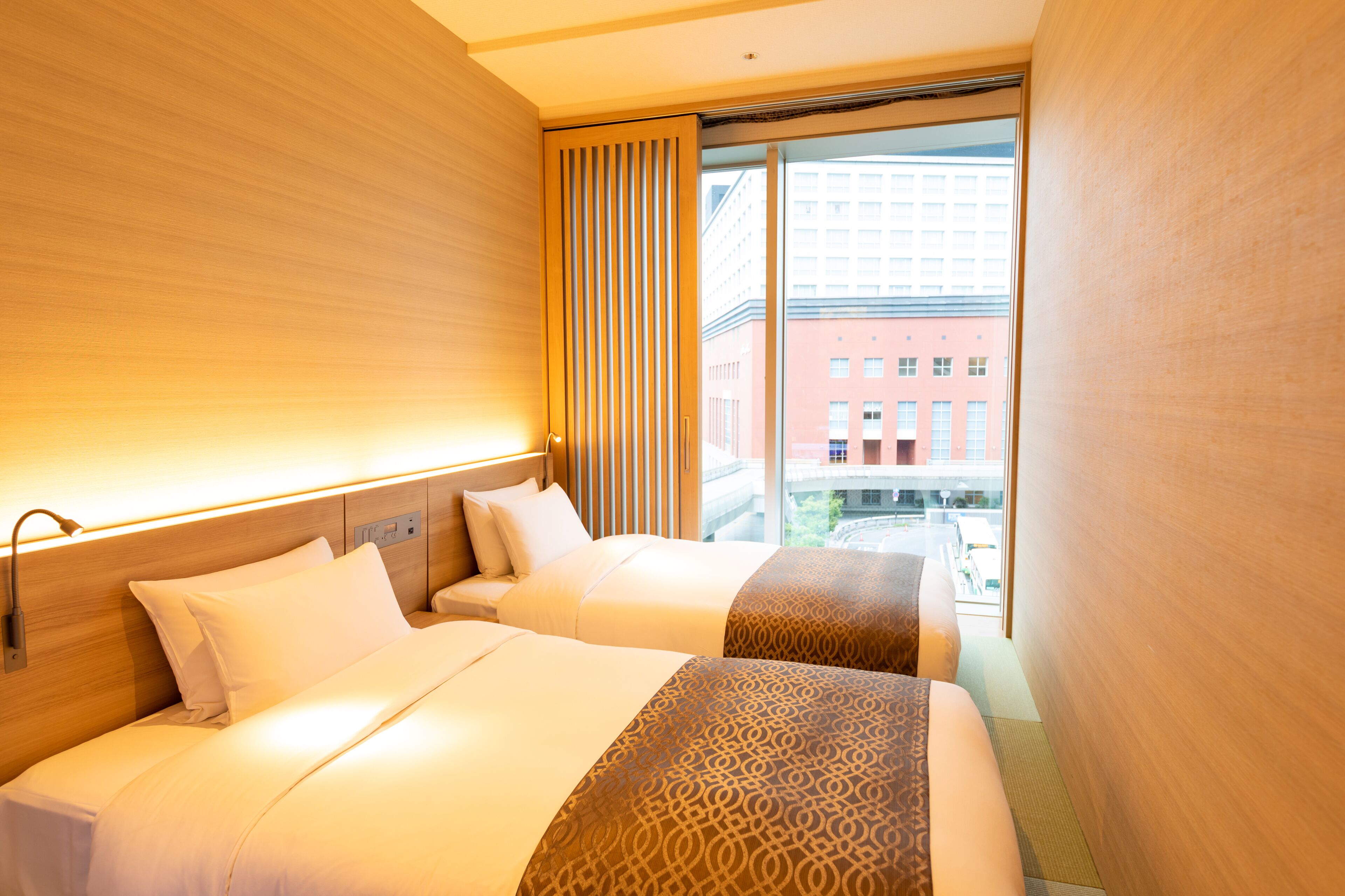 Quarto de hotel com duas camas, uma janela grande e vista para um edifício.