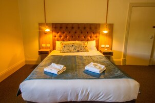 Quarto de hotel com uma cama grande, duas mesas de cabeceira e cabeceira com design acolchoado.