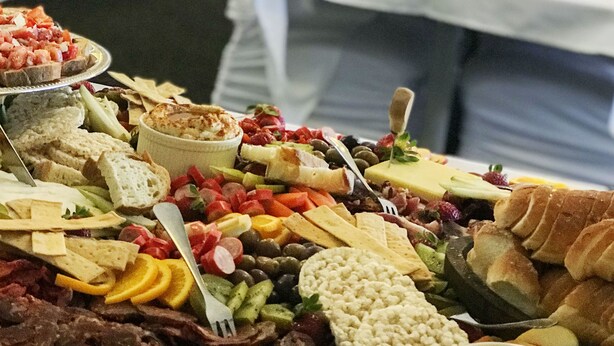 Uma mesa de buffet com diversos alimentos, incluindo queijos, frutas e carnes.