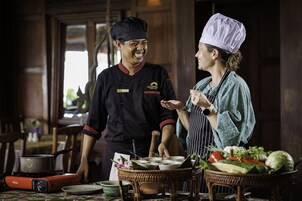 Um cozinheiro e uma mulher em uma cozinha, com um fogão, utensílios de cozinha e legumes frescos.