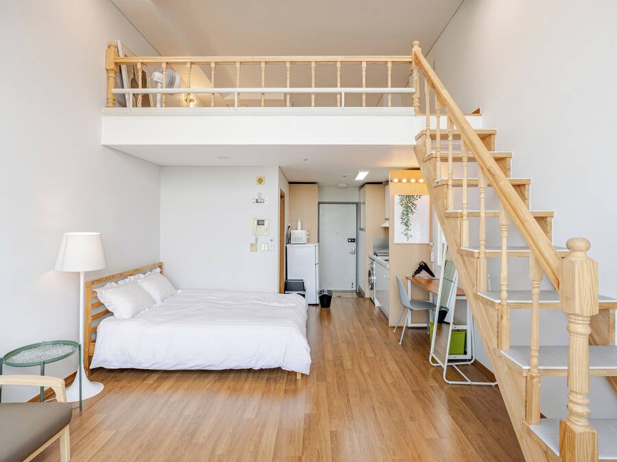 Um quarto amplo com um mezanino para dormir, escada de madeira, cama, escrivaninha e uma cadeira.