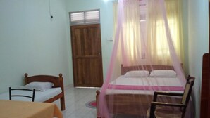 Quarto com cama sob um dossel rosa, porta de madeira e uma mesa com cadeira.