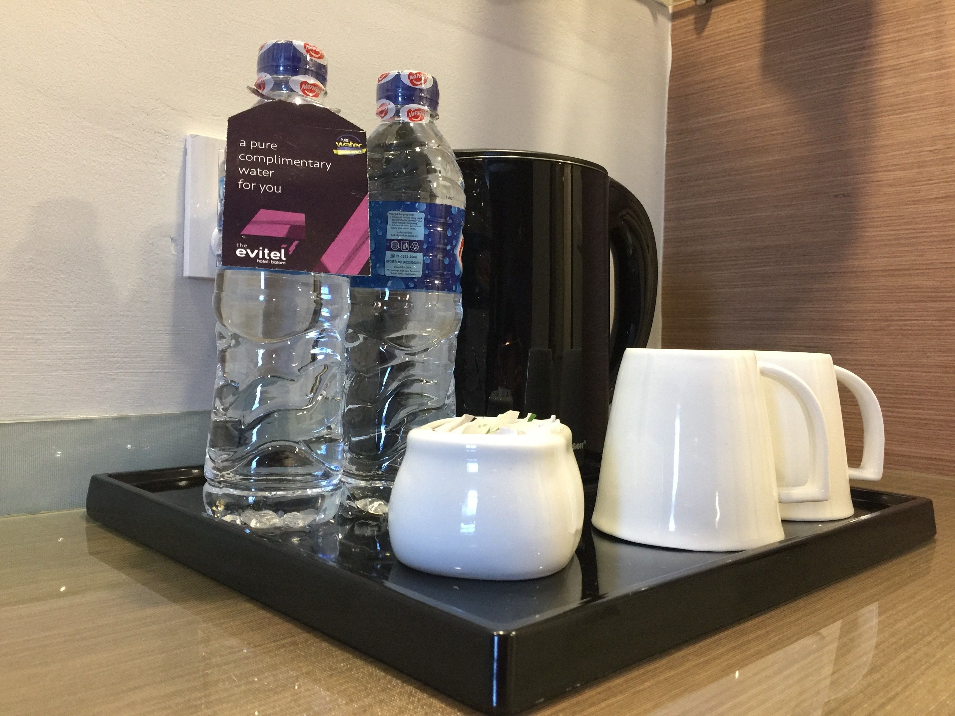 Uma bandeja com duas garrafas de água, uma cafeteira e duas canecas brancas sobre um balcão de hotel.