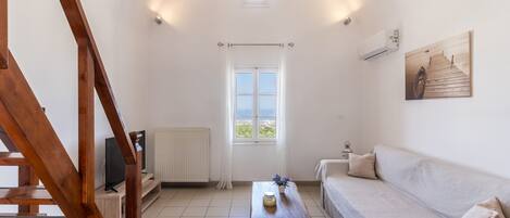 Uma sala de estar espaçosa com escada de madeira, um sofá branco, uma mesa de centro e uma janela com vista.