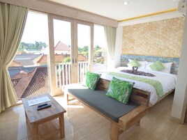 Quarto com cama, um banquinho, uma mesa e vista para o exterior.