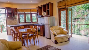 Uma cozinha espaçosa com armários de madeira, uma sala de jantar com mesa e cadeiras redondas, e uma varanda com vista para o verde.