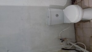 Casa de banho com sanita branca, tubagens visíveis e parede revestida a mosaicos.