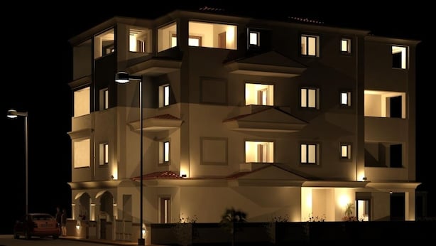 Um hotel de vários andares com janelas e varandas iluminadas, entrada visível e um poste de luz próximo.