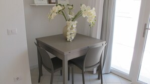 Uma mesa de jantar com quatro cadeiras, um vaso com flores brancas e uma prateleira na parede com quadros e uma cesta.