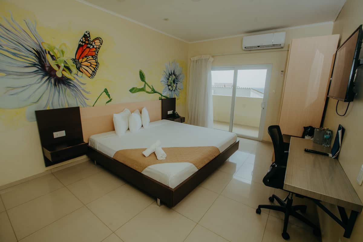 Quarto de hotel com cama, escrivaninha, cadeira, televisão e varanda com vista.