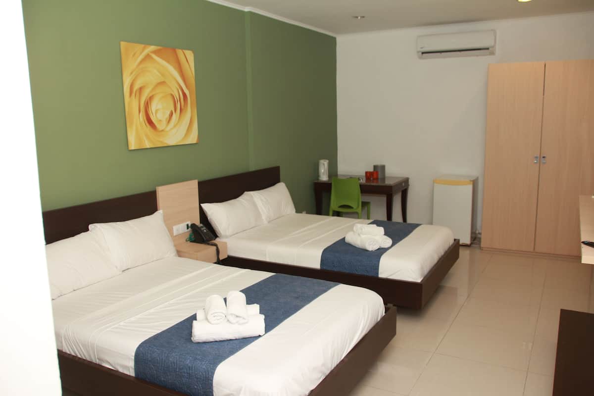 Quarto de hotel com duas camas, parede verde, um quadro, uma mesa com cadeira e um guarda-roupa.