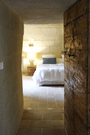 Corredor estreito que leva a um quarto com cama, mesa de cabeceira e abajur.