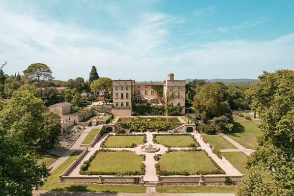 Um grande edifício histórico com um jardim de layout simétrico, incluindo uma fonte central e gramados bem cuidados.