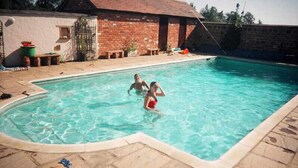 Piscina com duas pessoas na água, cercada por um edifício de tijolos e um muro de pedra.