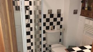 Casa de banho com chão xadrez, cabine de chuveiro em vidro, sanita e lavatório.