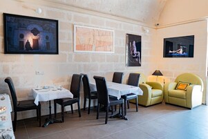 Uma sala de jantar com mesa posta para dois, um sofá e obras de arte nas paredes.