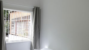 Quarto com uma cama de solteiro, ventilador de teto e janela com cortinas.