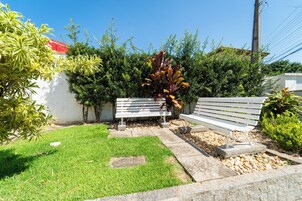 Um jardim bem cuidado com gramado, um banco branco e diversos arbustos e plantas.