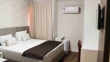 Quarto de hotel com cama, mesa de cabeceira, cadeira, ar condicionado e televisão fixada na parede.