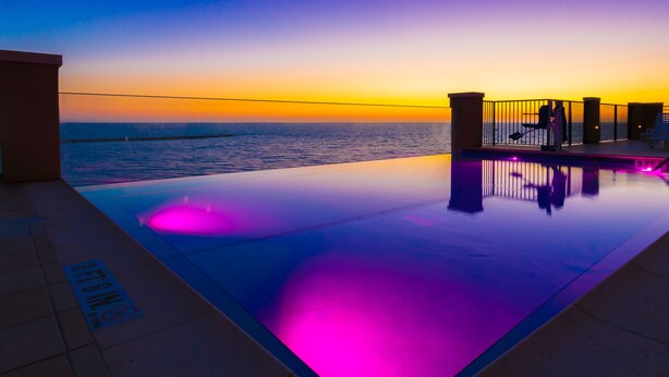 Piscina infinita com vista para o oceano ao pôr do sol, um corrimão e uma placa indicando profundidade de 91 centímetros.