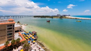 Um hotel na praia com área de piscina, guarda-sóis e vista para o oceano e uma ponte ao longe.