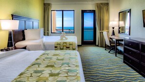 Quarto de hotel com duas camas, uma escrivaninha, uma cadeira, cômoda e vista para o oceano pelas janelas.