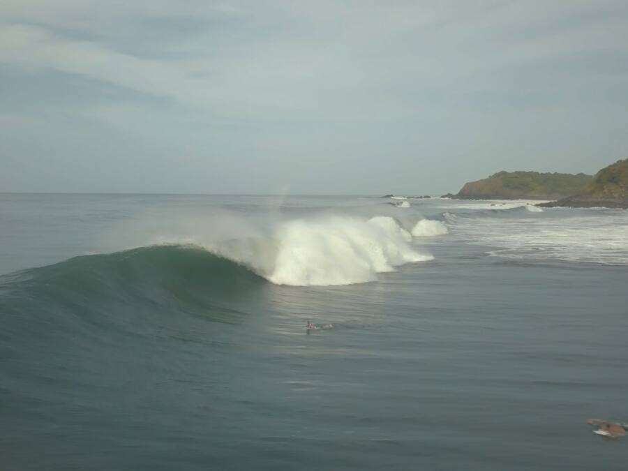 Uma praia com ondas e um afloramento rochoso ao longe.