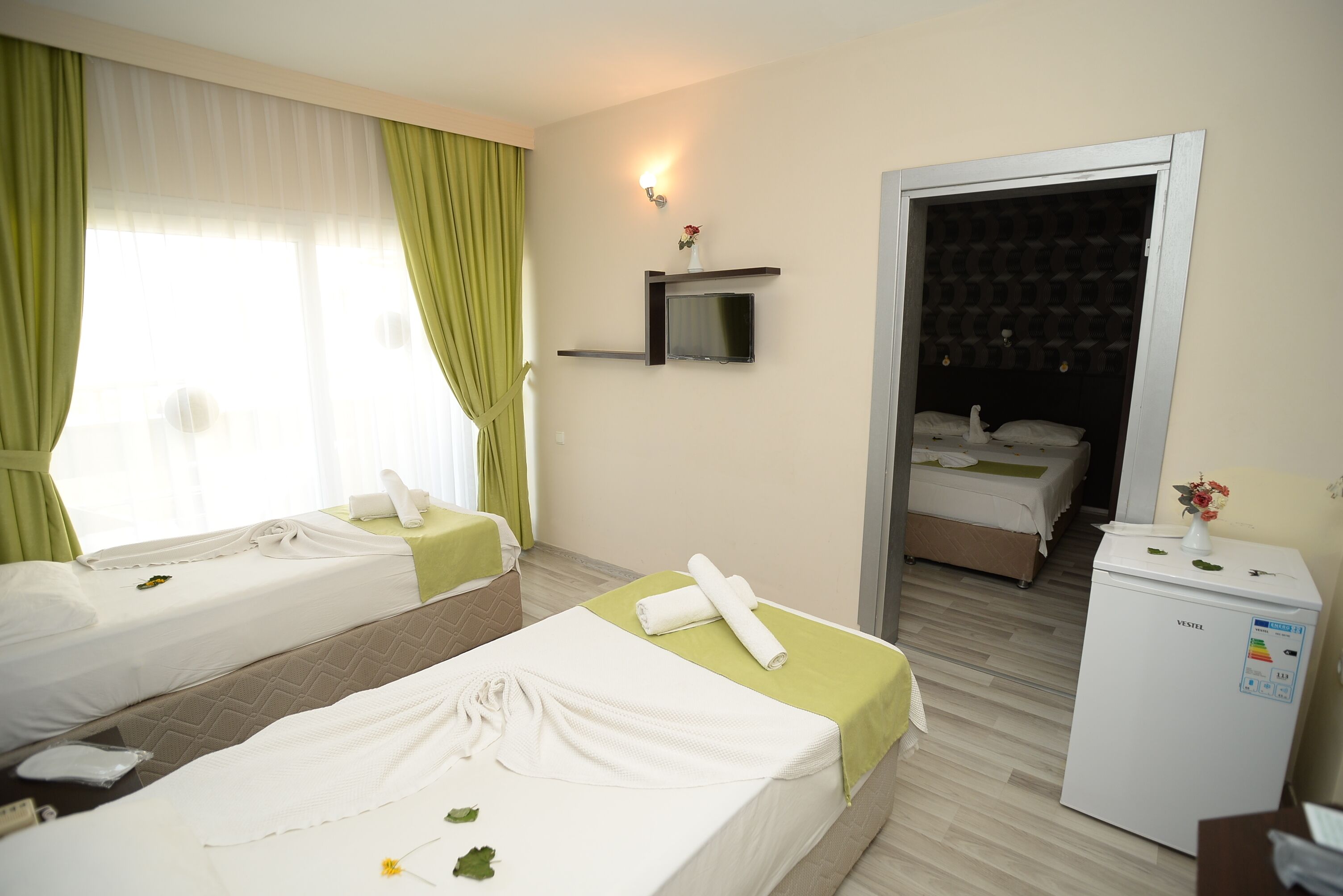Quarto de hotel com duas camas, televisão, frigorífico e banheiro visível por uma porta aberta.