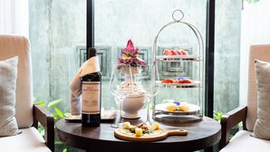 Uma mesa com uma garrafa de Merlot, um vaso com flores e um suporte escalonado para doces com pastelaria.