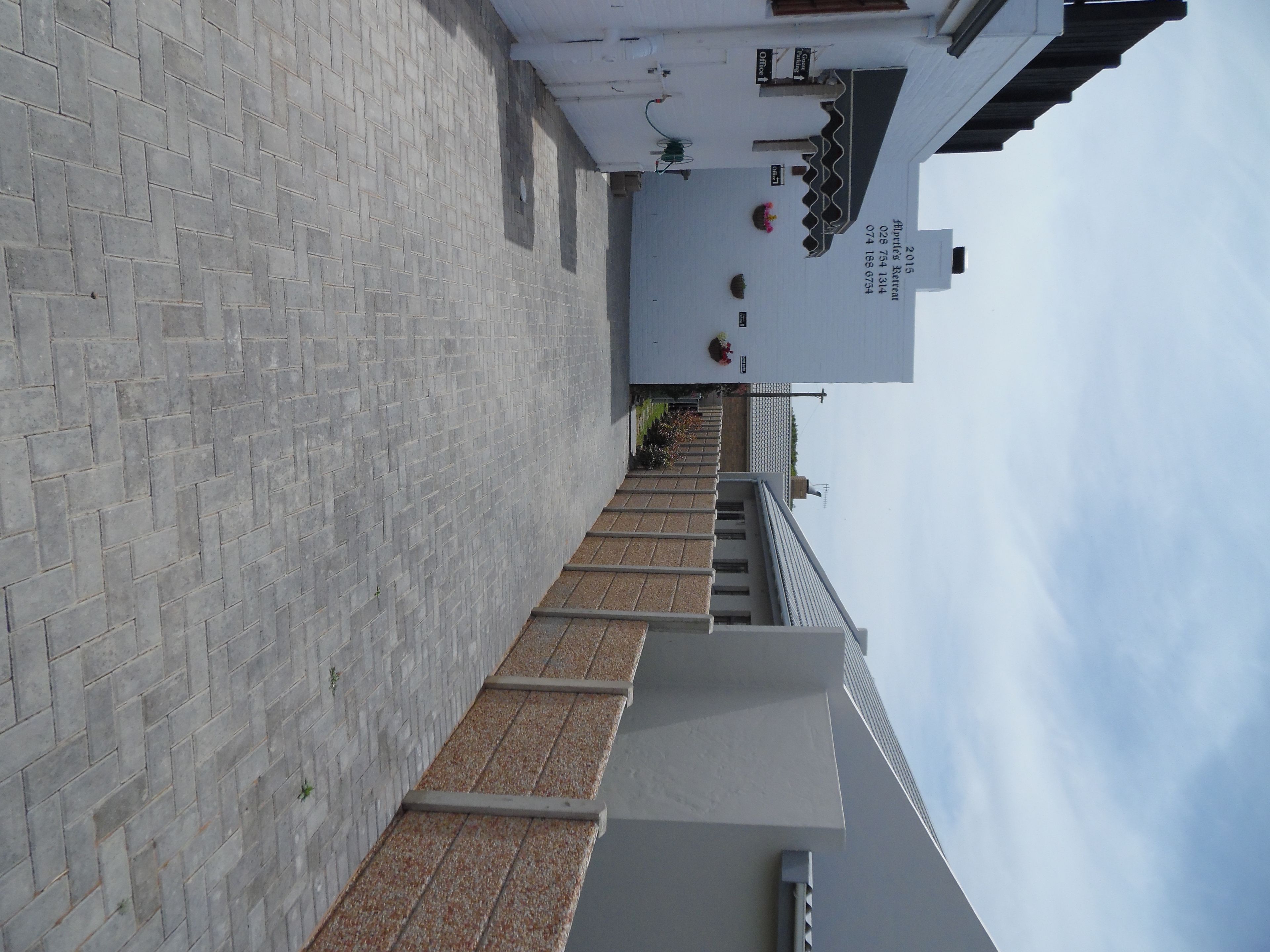 Uma trilha que leva a um edifício com fachada branca e uma placa com o ano 2013.