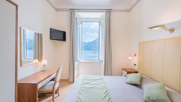 Quarto de hotel com cama, escrivaninha, cadeira, televisão, janela com vista para as montanhas e abajur.