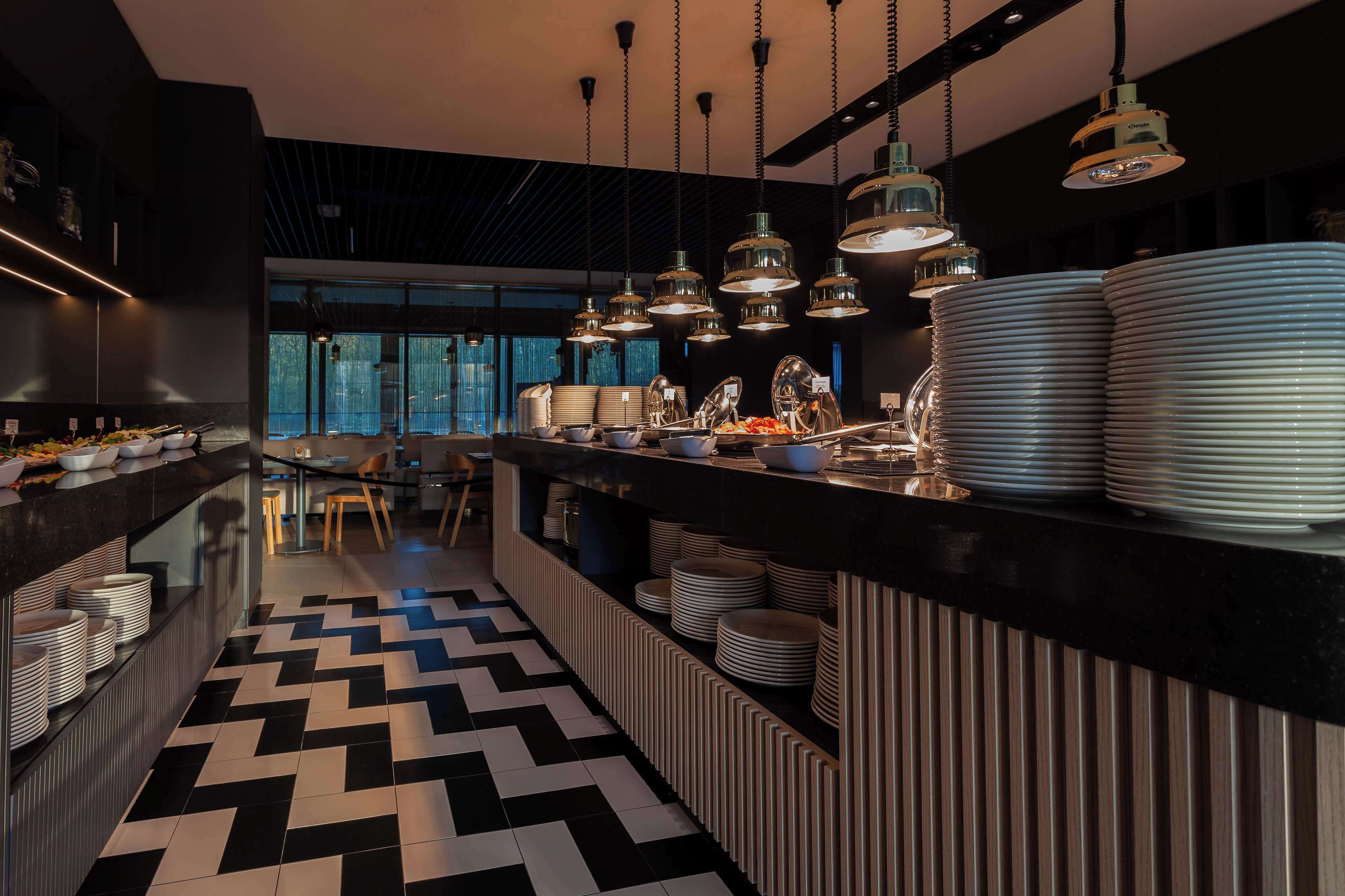 Uma cozinha moderna com piso em padrão geométrico preto e branco, eletrodomésticos de aço inoxidável e luminárias pendentes.