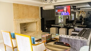 Uma sala de estar moderna com uma mesa de centro de vidro, poltronas estofadas, um sofá cinzento e uma TV de tela plana fixada na parede.