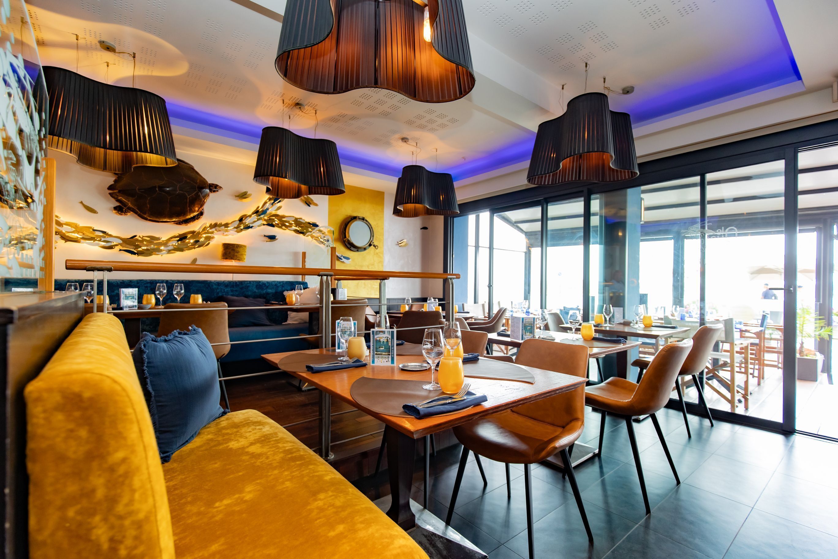 Restaurante moderno com sofás amarelos, mesas de madeira e luminárias pendentes pretas.
