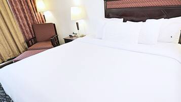 Quarto de hotel com uma cama grande, uma cadeira, duas mesinhas de cabeceira e luminárias.