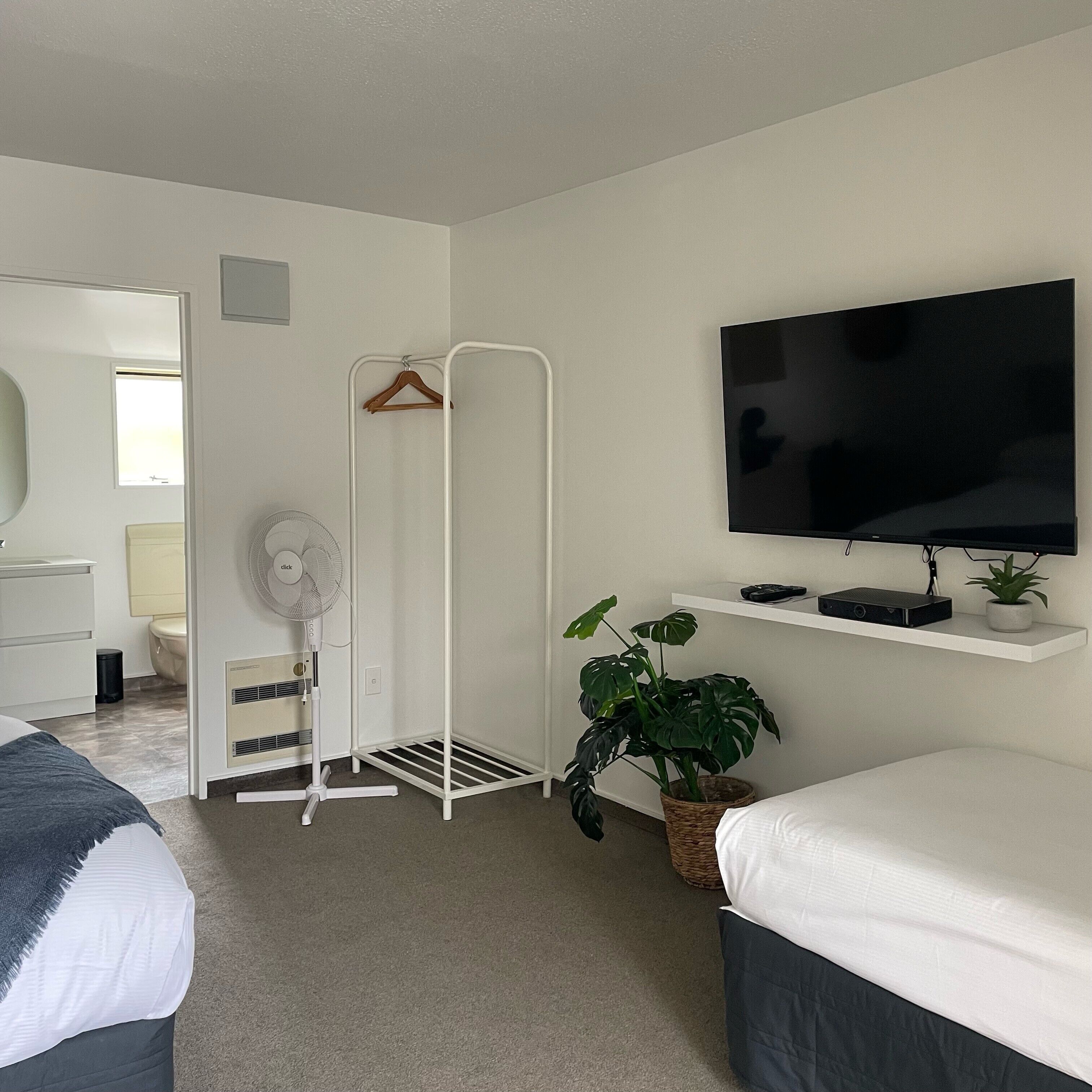 Quarto de hotel moderno com uma cama, uma TV, uma planta e um varal.