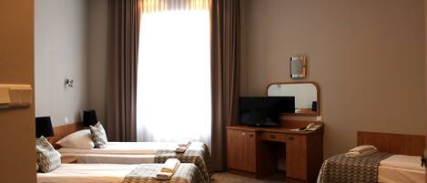 Quarto de hotel com duas camas, uma escrivaninha com televisão e uma janela grande com cortinas.