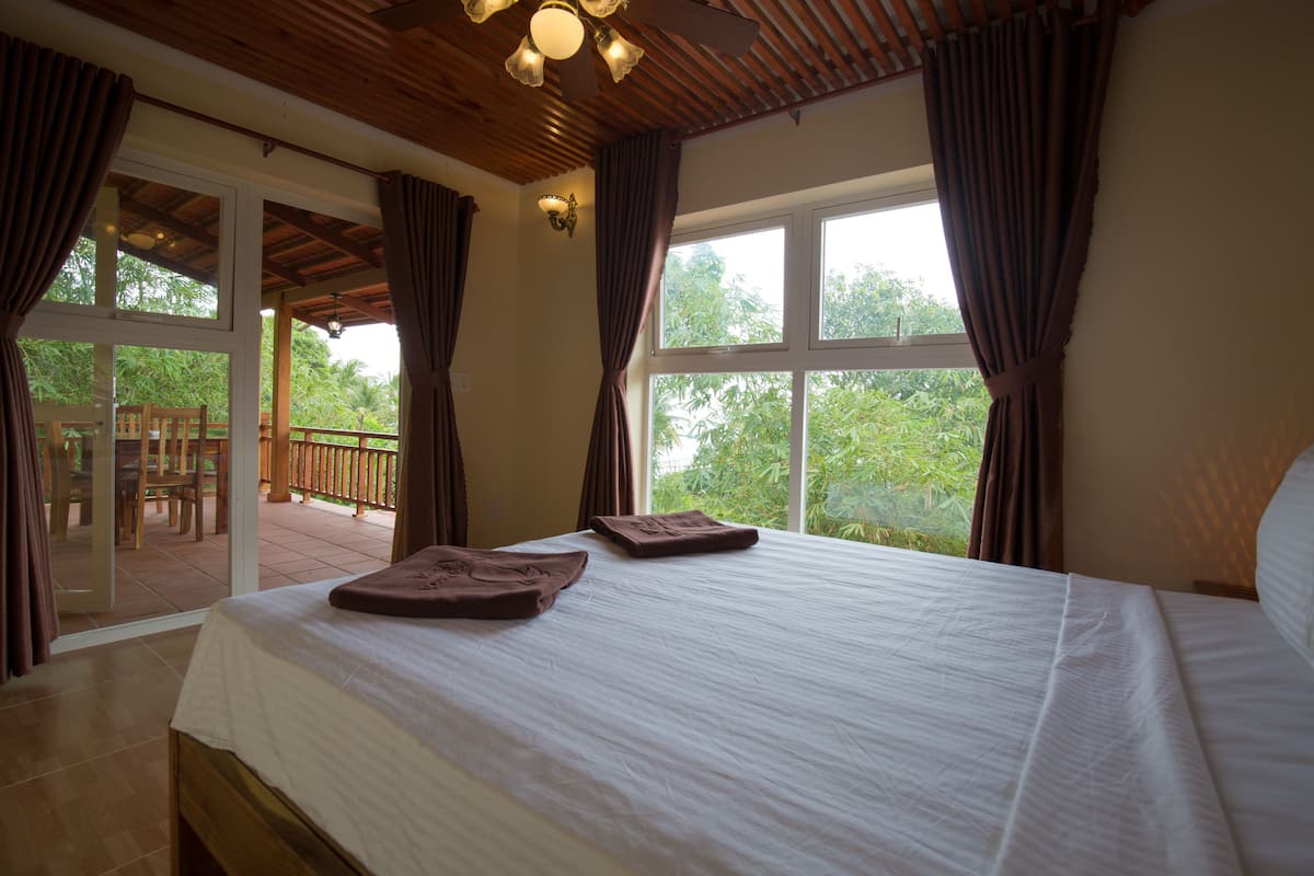 Quarto com cama, cortinas e vista para o verde lá fora.
