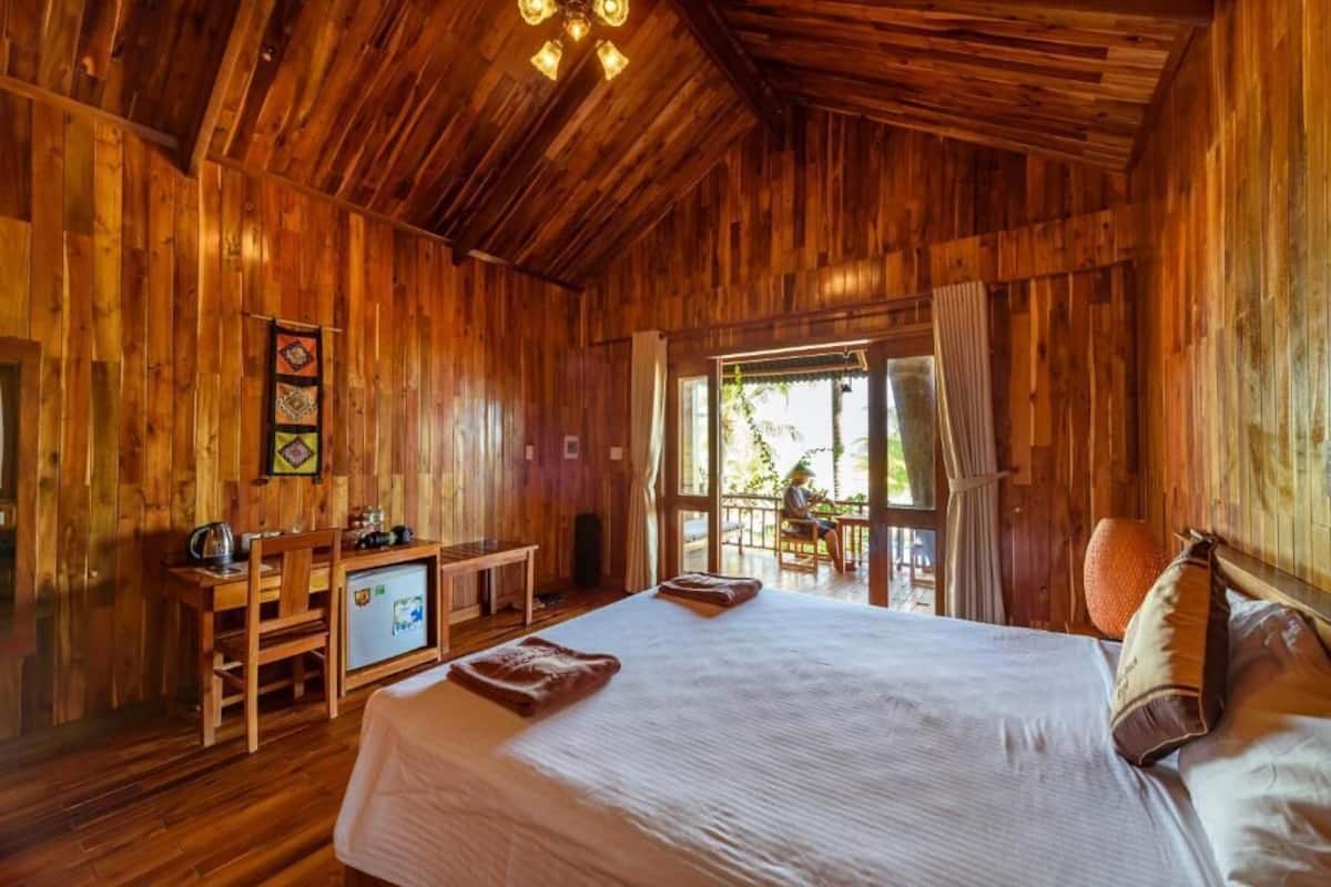Quarto de madeira com uma cama, uma escrivaninha e uma janela.